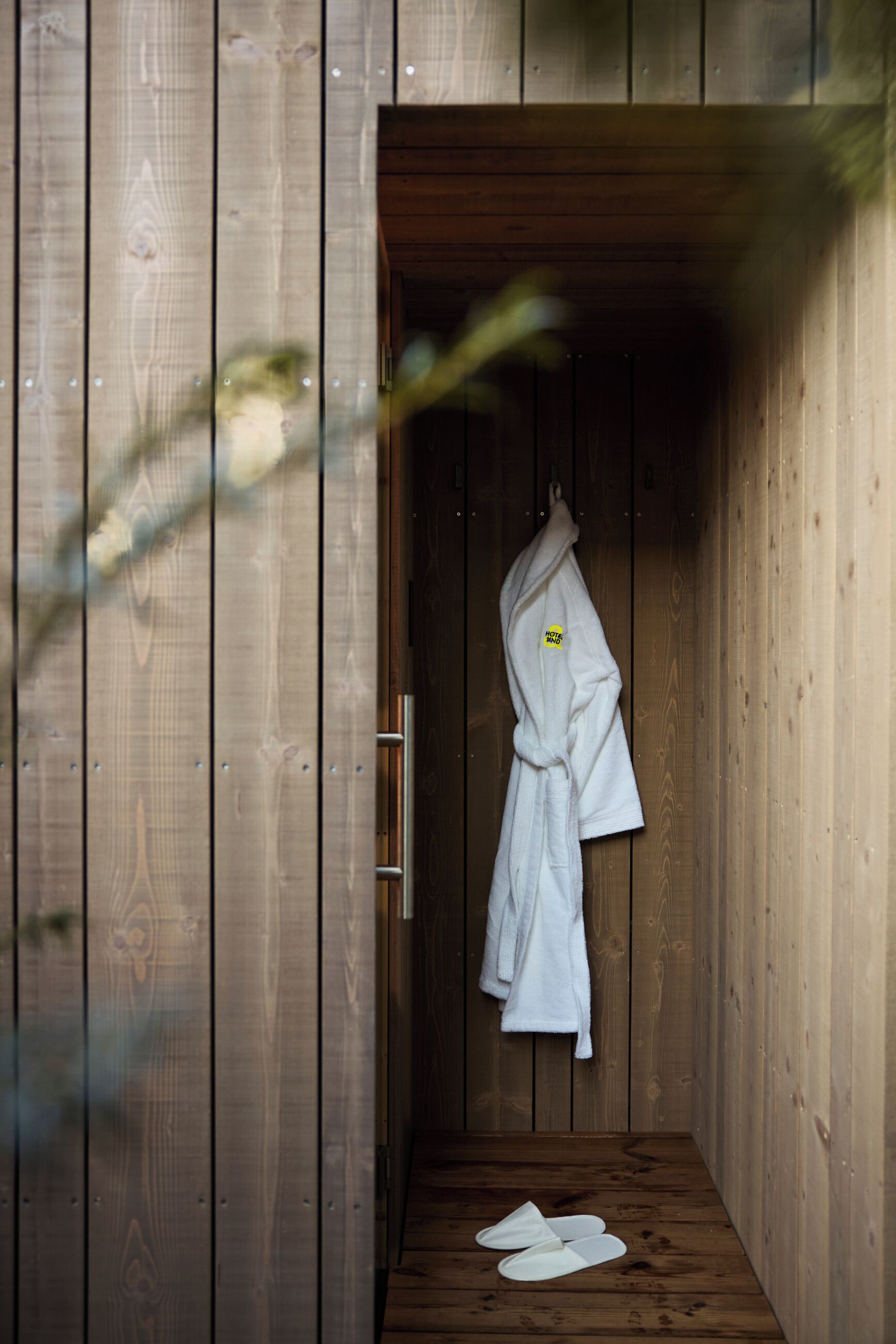 Uma sauna de madeira com um roupão branco pendurado na parede e um par de chinelos no chão.