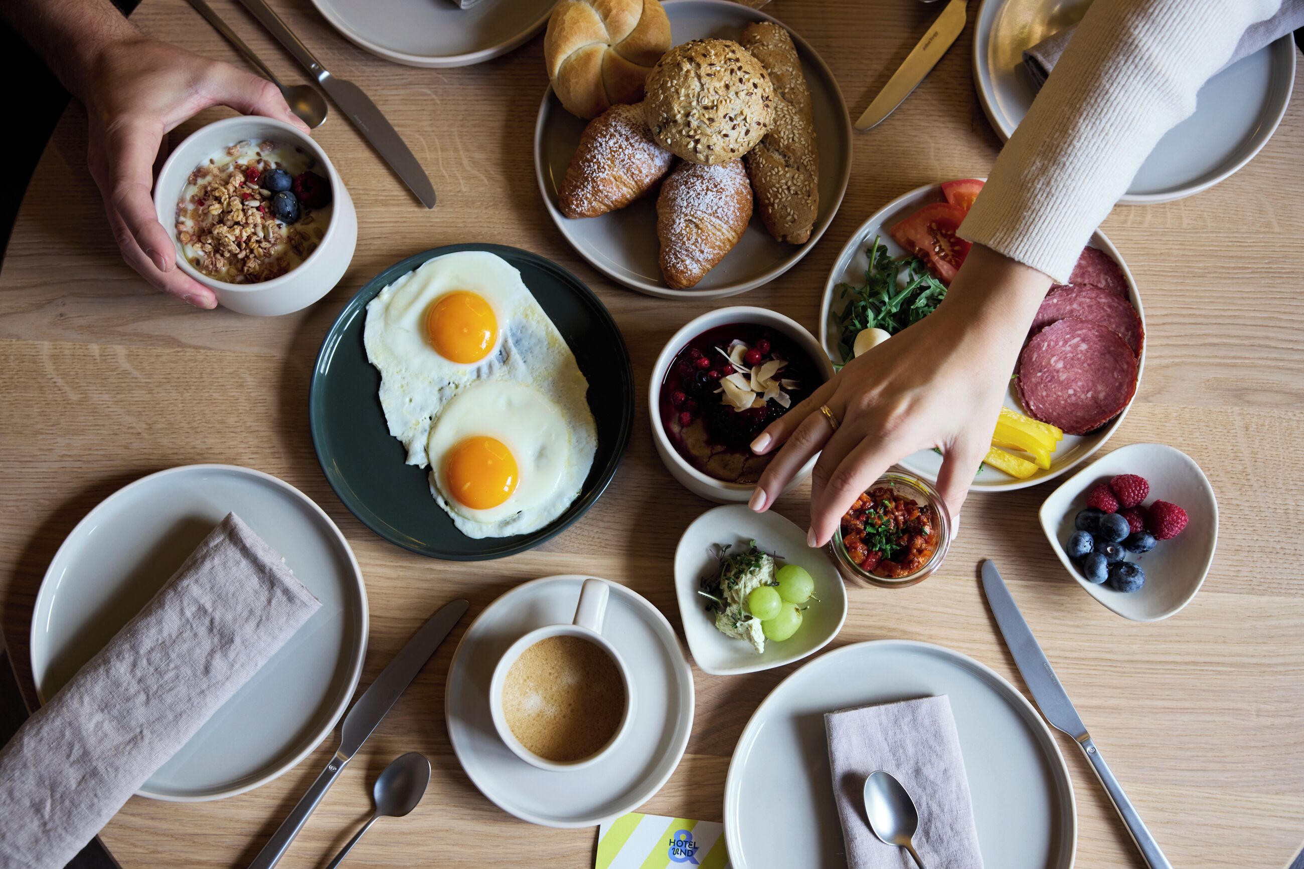 Mesa de café da manhã com diversos pratos, incluindo ovos, pão, frutas vermelhas e uma fatia de bolo.