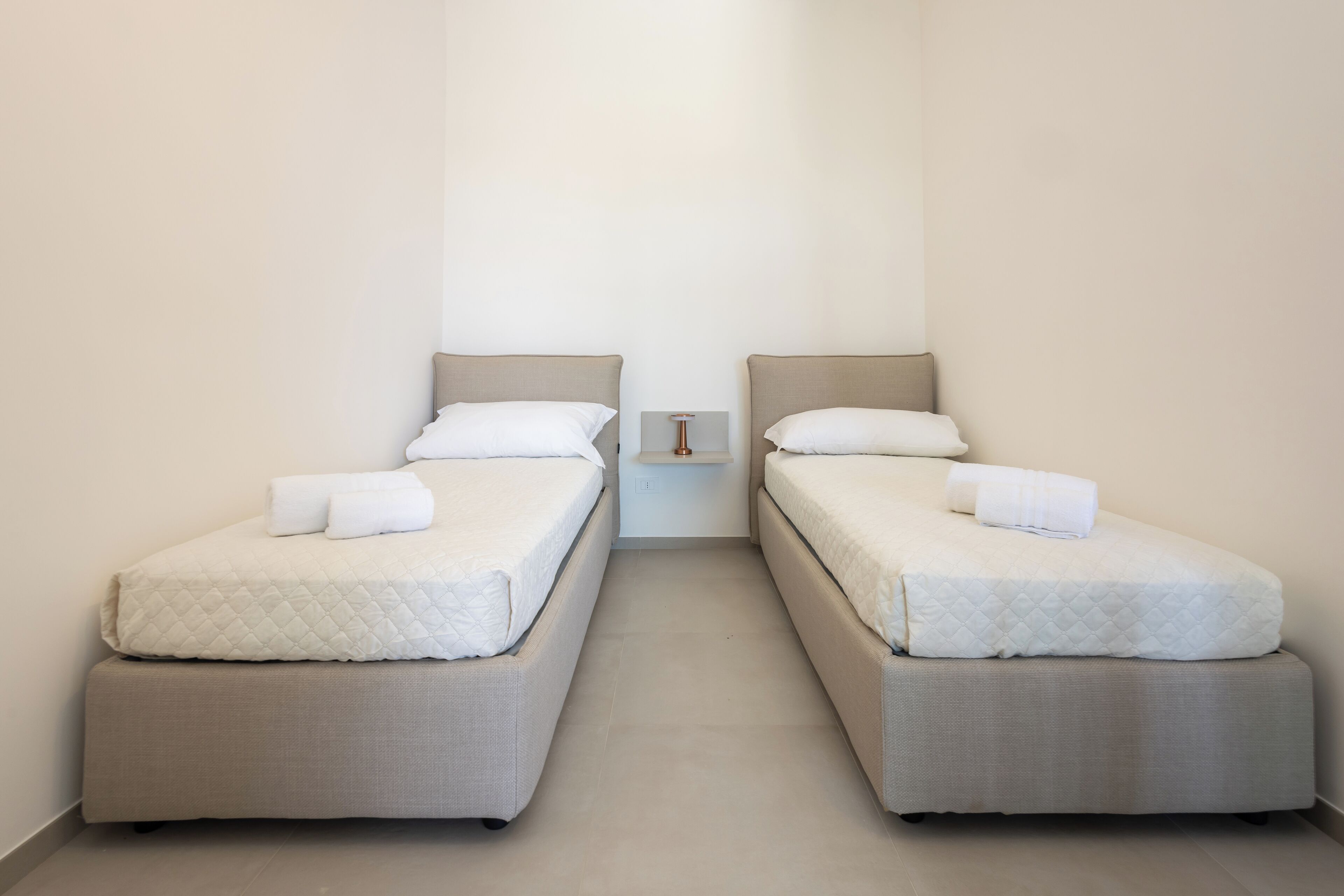 Quarto duplo com duas camas, cada uma com travesseiro e toalha dobrada.
