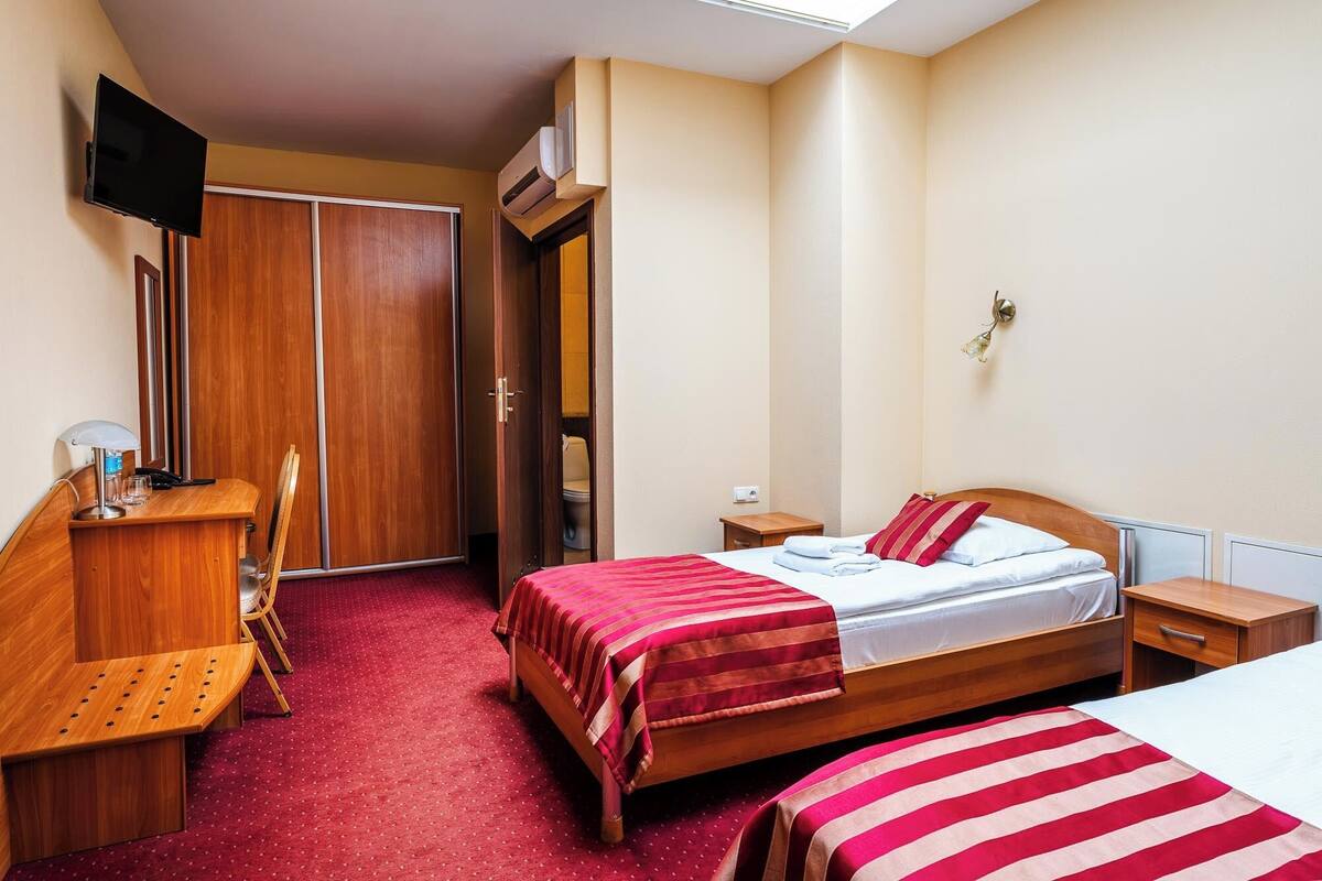 Quarto de hotel com cama, mesas de cabeceira, escrivaninha com cadeira, televisão e ar condicionado.