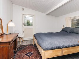 Quarto com cama de madeira, escrivaninha com luminária, cadeira e tapete estampado.