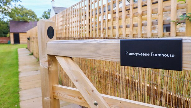 Uma cerca de madeira com uma placa que diz 'Preesgweene Farmhouse'.
