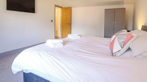Quarto de hotel com uma cama grande, um guarda-roupa, uma TV de tela plana fixada na parede e uma porta que dá para outro quarto.
