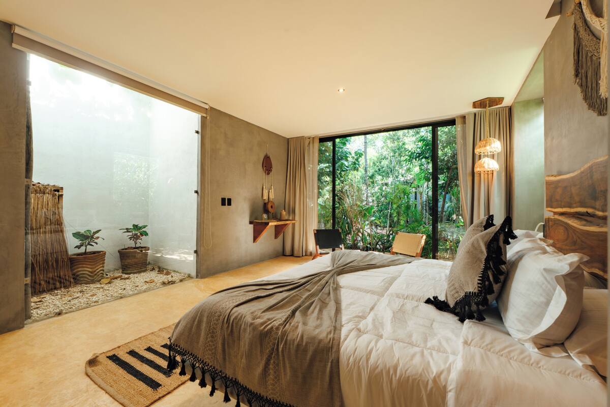 Quarto moderno com uma cama grande, vista para o verde pela janela e decoração minimalista.