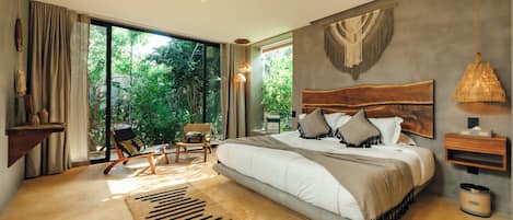 Quarto moderno com uma cama grande, cabeceira de madeira, vista para o verde através de amplas janelas e um espaço de estar acolhedor com uma poltrona e um tapete.