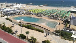 Um resort à beira-mar com uma grande piscina, espreguiçadeiras e guarda-sóis.