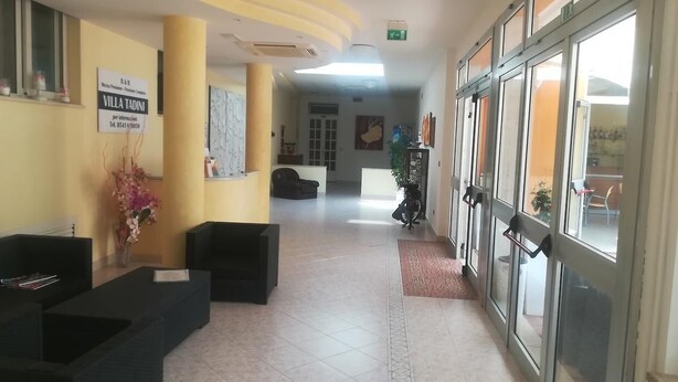 Um lobby de hotel com sofás pretos, um balcão de recepção e uma placa com a inscrição 'Villa Tadim'.