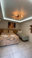 Quarto com cama, um banquinho, um quadro e luminária no teto.