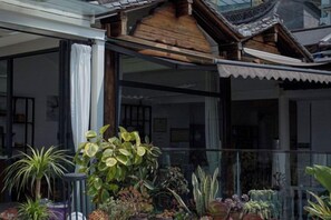 Um edifício em estilo tradicional japonês, com fachada de madeira, amplas janelas de vidro e diversos vasos de plantas.