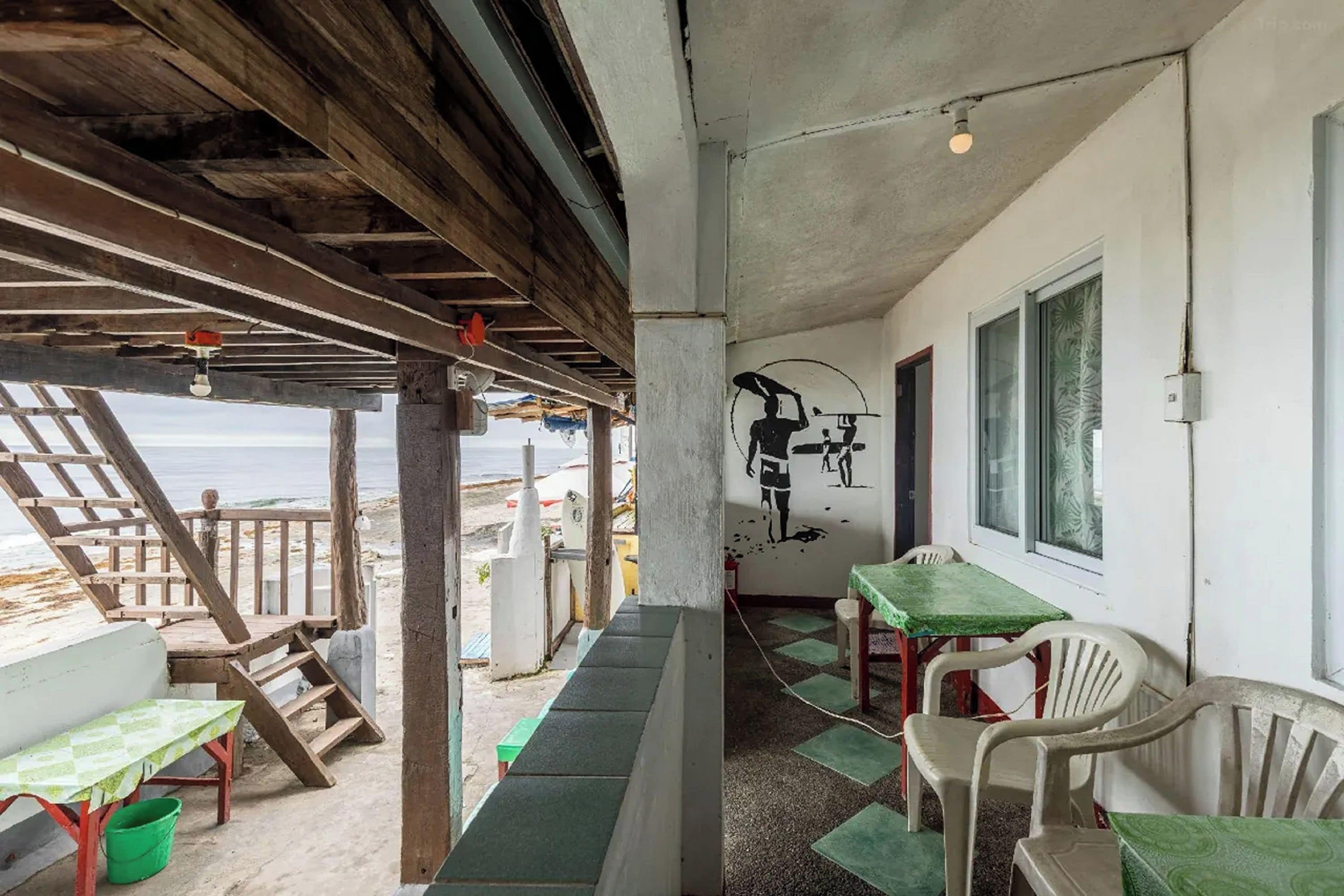 Um café à beira-mar com mesas ao ar livre, um mural e vista para o mar.