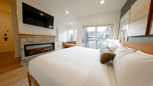 Quarto com uma cama grande, lareira de pedra, TV fixada na parede e varanda com vista para a cidade.