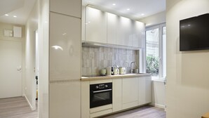Cozinha moderna com armários brancos, forno embutido e janela que traz luz natural.