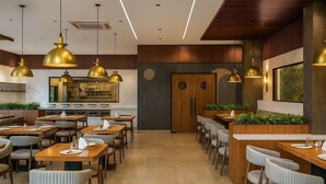 Interior moderno de restaurante com mesas e cadeiras de madeira, iluminação pendente e um balcão central.