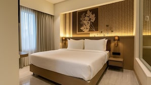 Quarto de hotel moderno com uma cama grande, uma mesa de cabeceira, um abajur e um painel decorativo na parede.