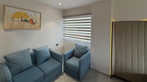 Uma sala de estar moderna com um sofá azul, um quadro abstrato grande e uma janela com persianas.