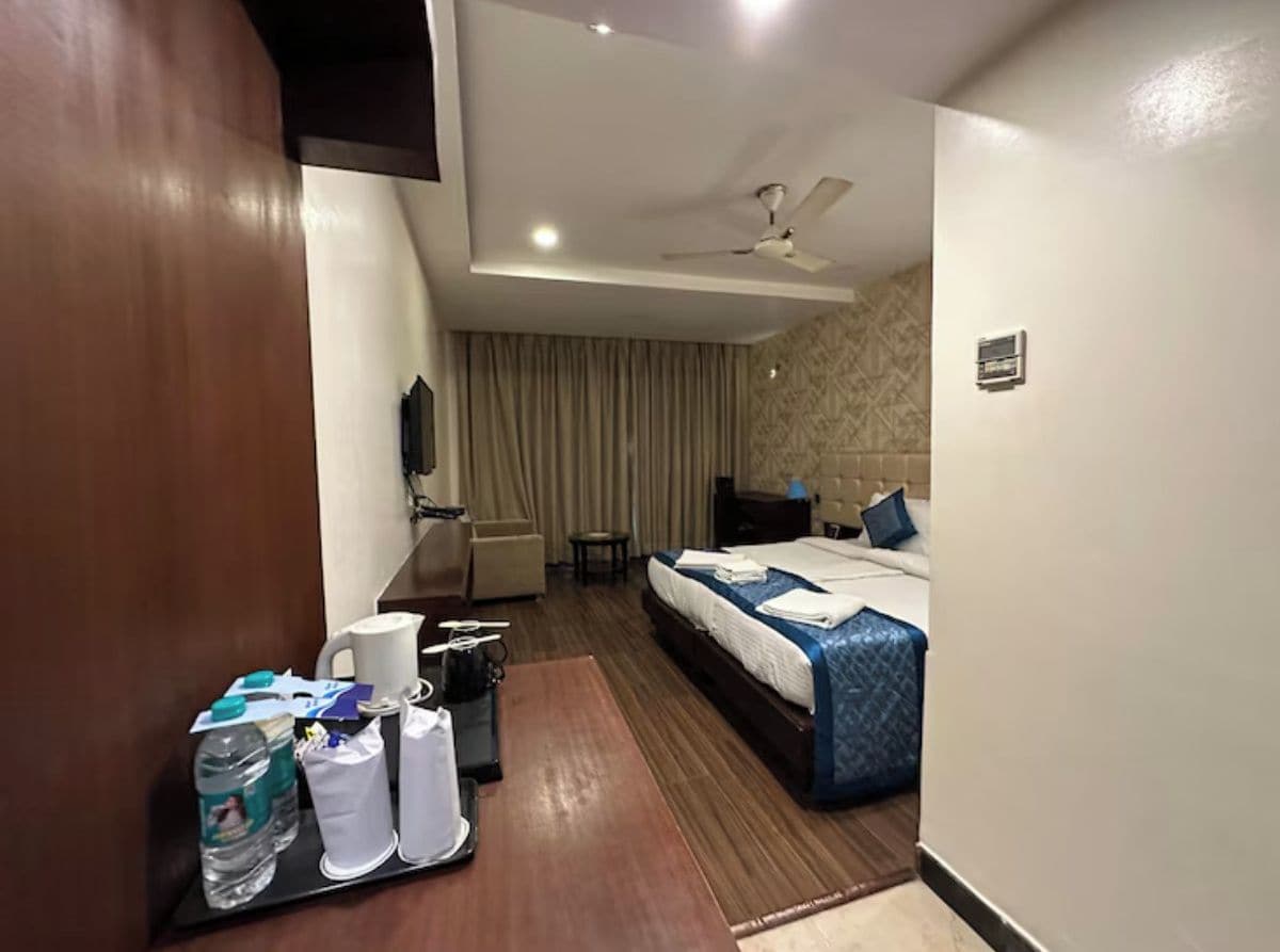 Quarto de hotel com cama, escrivaninha com cadeira, mesinha e ventoinha no teto. Há artigos de higiene pessoal na escrivaninha.