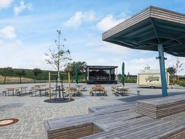 Área externa com mesas, bancos, um palco e um caminhão com a inscrição 'Dithmarscher Pilsener'.