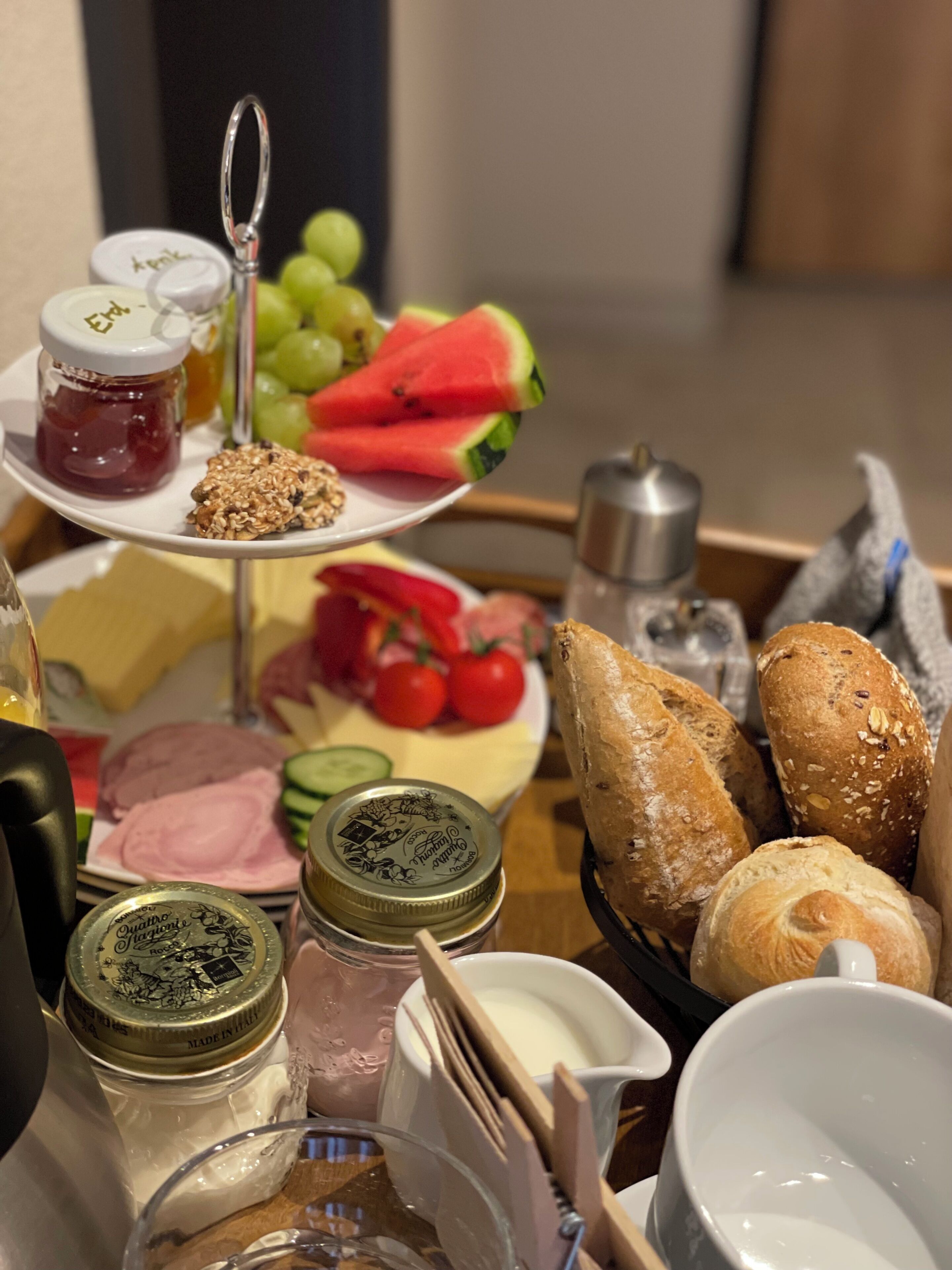 Um buffet de café da manhã com diversos alimentos, incluindo pães, queijos, frutas e acompanhamentos.