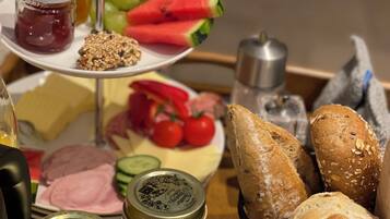 Um buffet de café da manhã com diversos alimentos, incluindo pães, queijos, frutas e acompanhamentos.