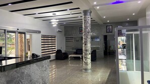 Uma área de recepção moderna com um balcão de mármore, um pilar imponente e uma área de estar com sofá e cadeiras.