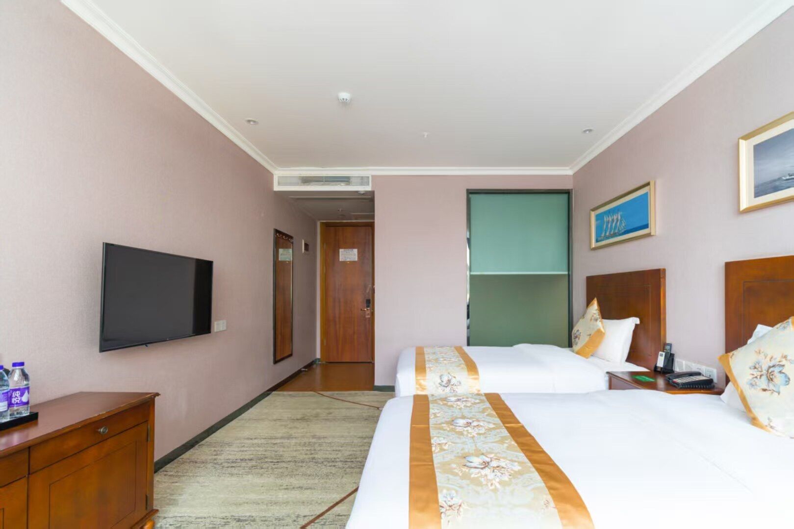 Quarto de hotel com duas camas, uma TV de tela plana, um penteado de madeira e uma parede verde.