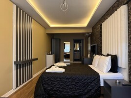 Quarto de hotel moderno com uma cama grande, uma mesa de cabeceira, um espelho e um banheiro visível por uma porta aberta.