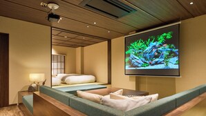Quarto de hotel moderno com uma cama grande, área de estar, televisão exibindo um aquário e teto de madeira.