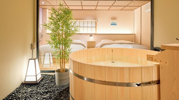 Quarto tradicional japonês com piso de tatame, banheira de madeira, planta de bambu e tela shoji deslizante.