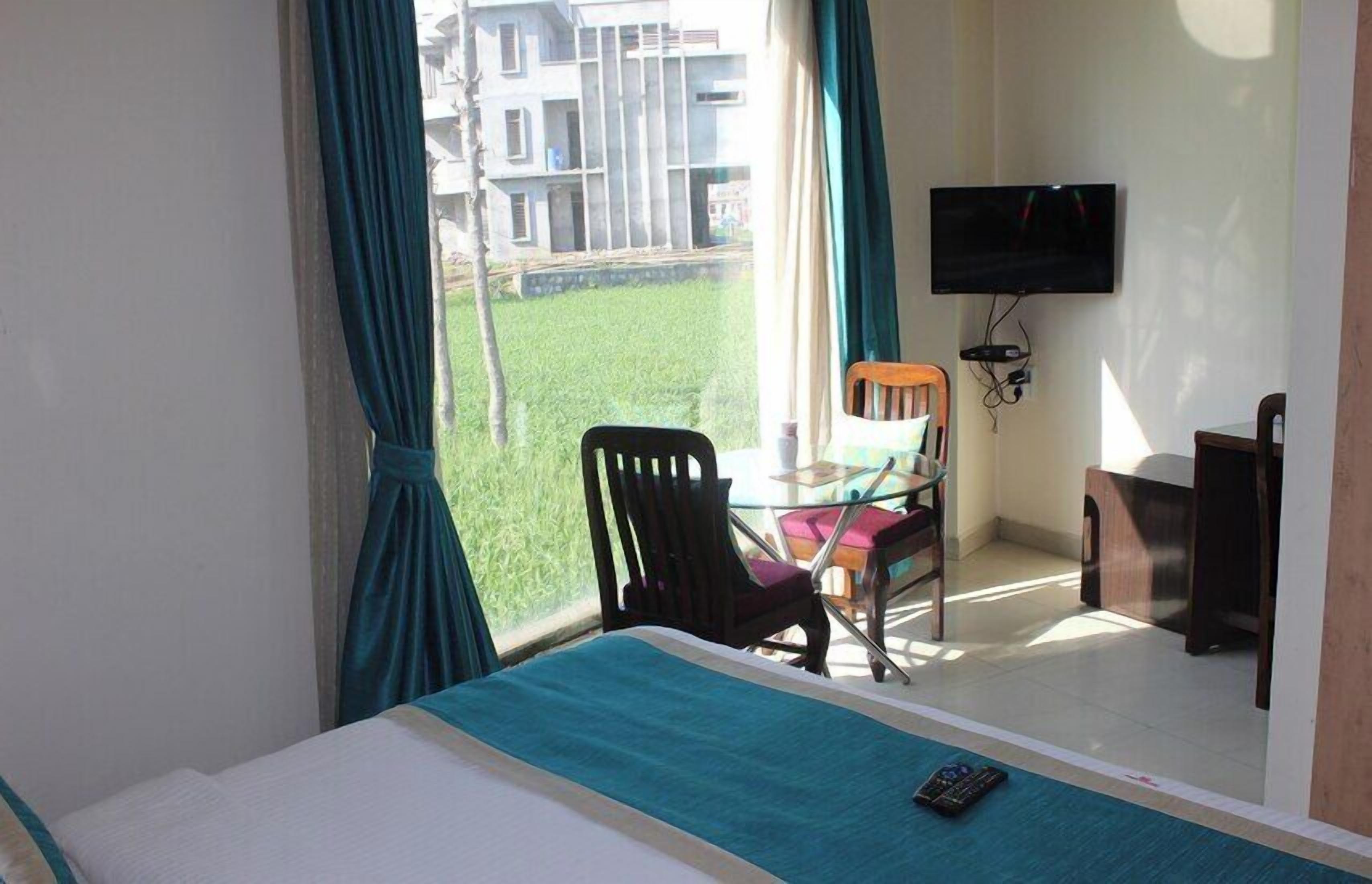Quarto de hotel com cama, televisão na parede, escrivaninha e cadeira.