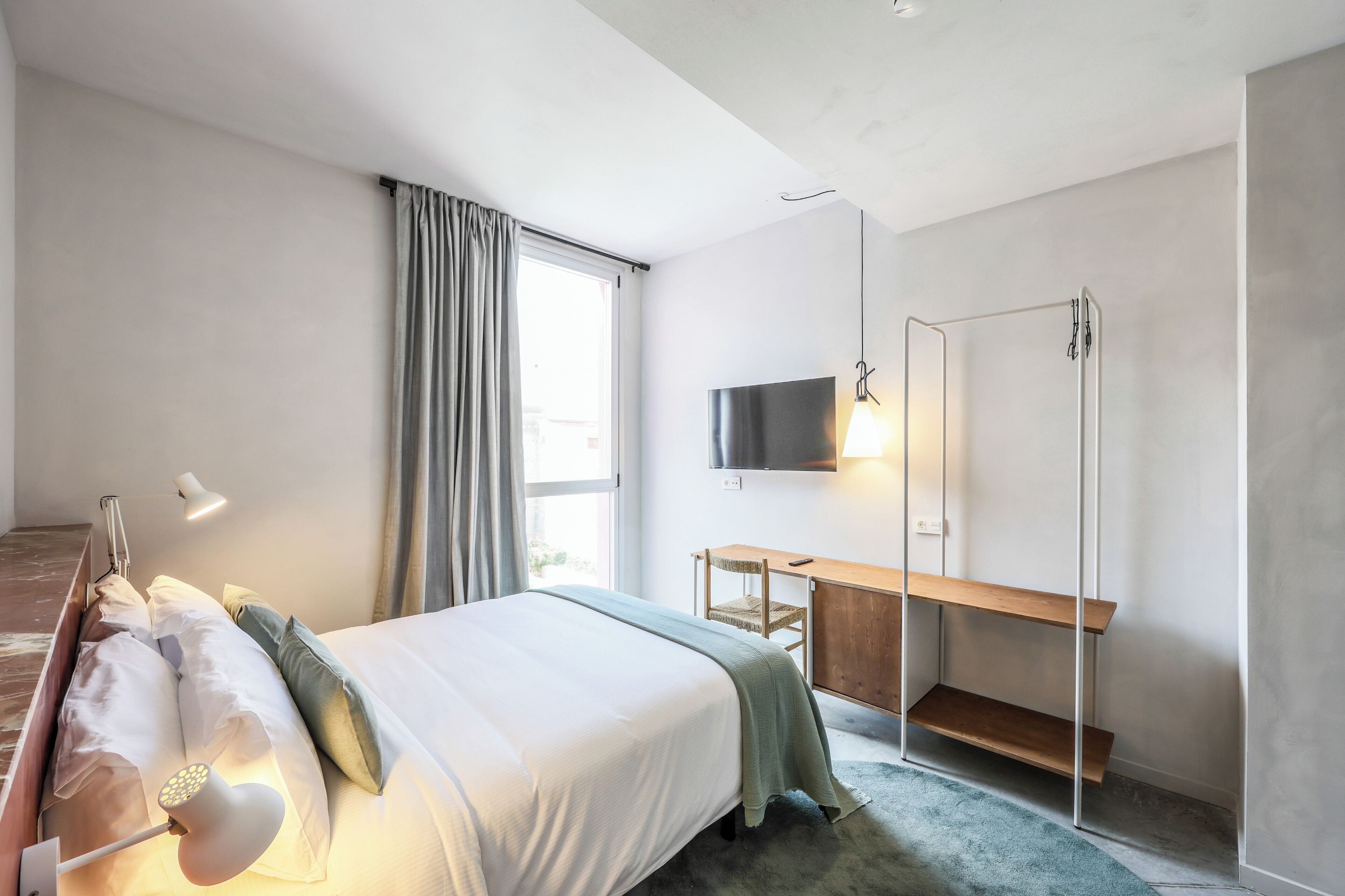 Quarto de hotel moderno com cama, mesa de cabeceira, cadeira, escrivaninha e um closet espaçoso.