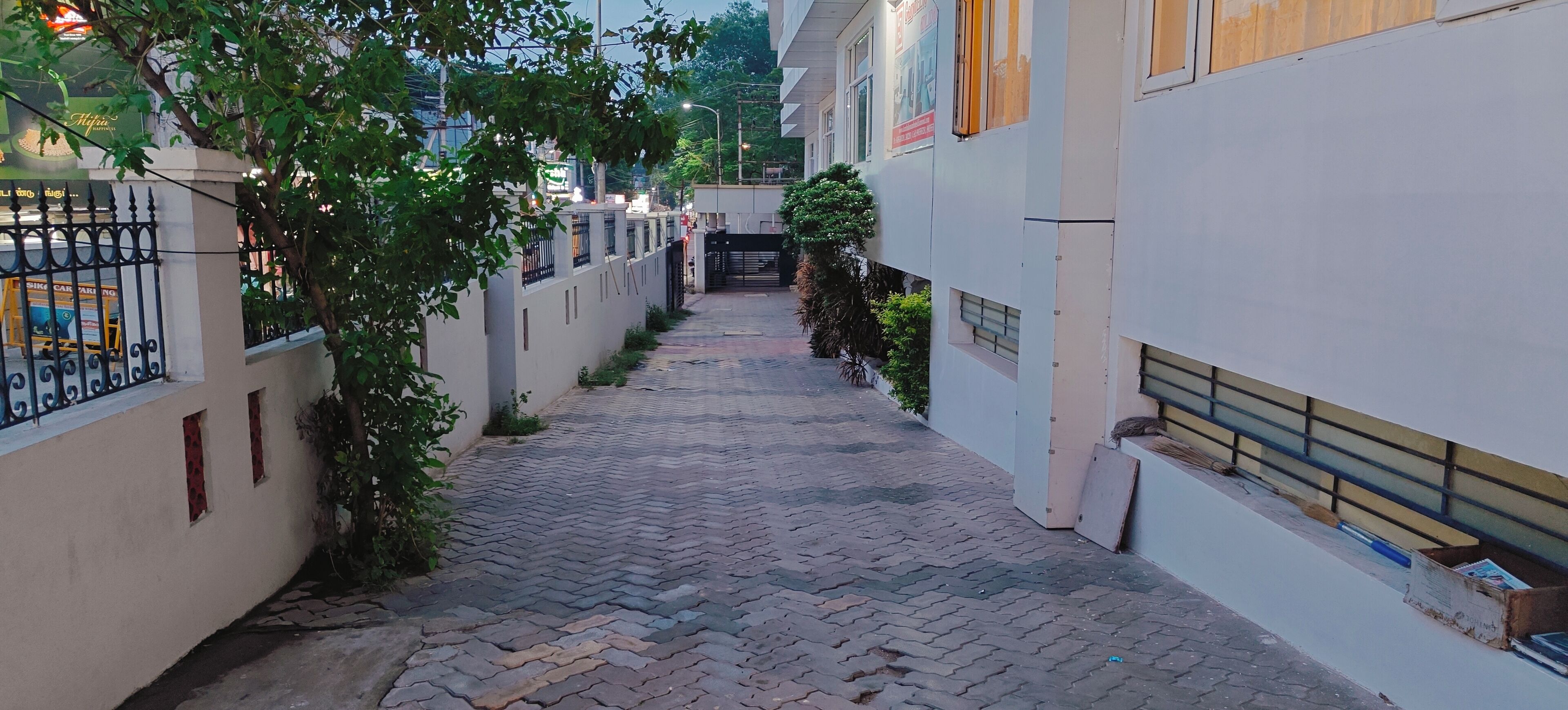 Um estreito beco pavimentado, ladeado por edifícios com grades nas janelas e um portão ao fundo.