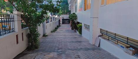 Um estreito beco pavimentado, ladeado por edifícios com grades nas janelas e um portão ao fundo.