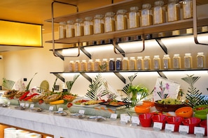 Buffet com diversos alimentos e acompanhamentos, incluindo potes de grãos e uma variedade de frutas e legumes frescos.