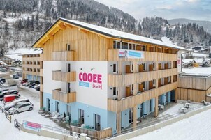 Um hotel com várias andares, fachada de madeira e varandas, rodeado por montanhas cobertas de neve.