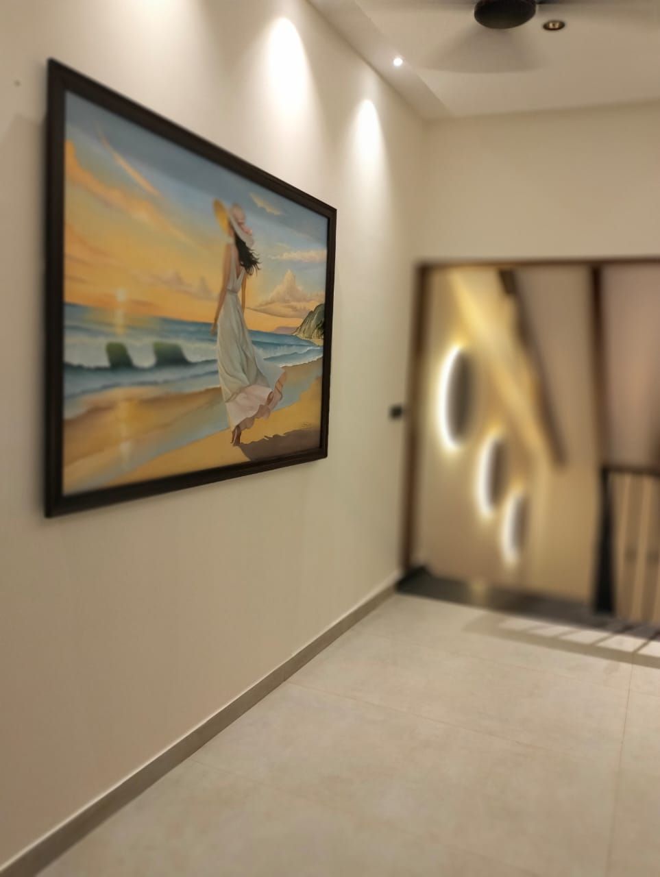 Um corredor com um quadro de uma mulher de vestido branco caminhando por uma praia ao pôr do sol.