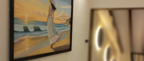Um corredor com um quadro de uma mulher de vestido branco caminhando por uma praia ao pôr do sol.