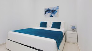 Quarto com cama, almofadas, mesa de cabeceira, luminária e uma obra de arte na parede.