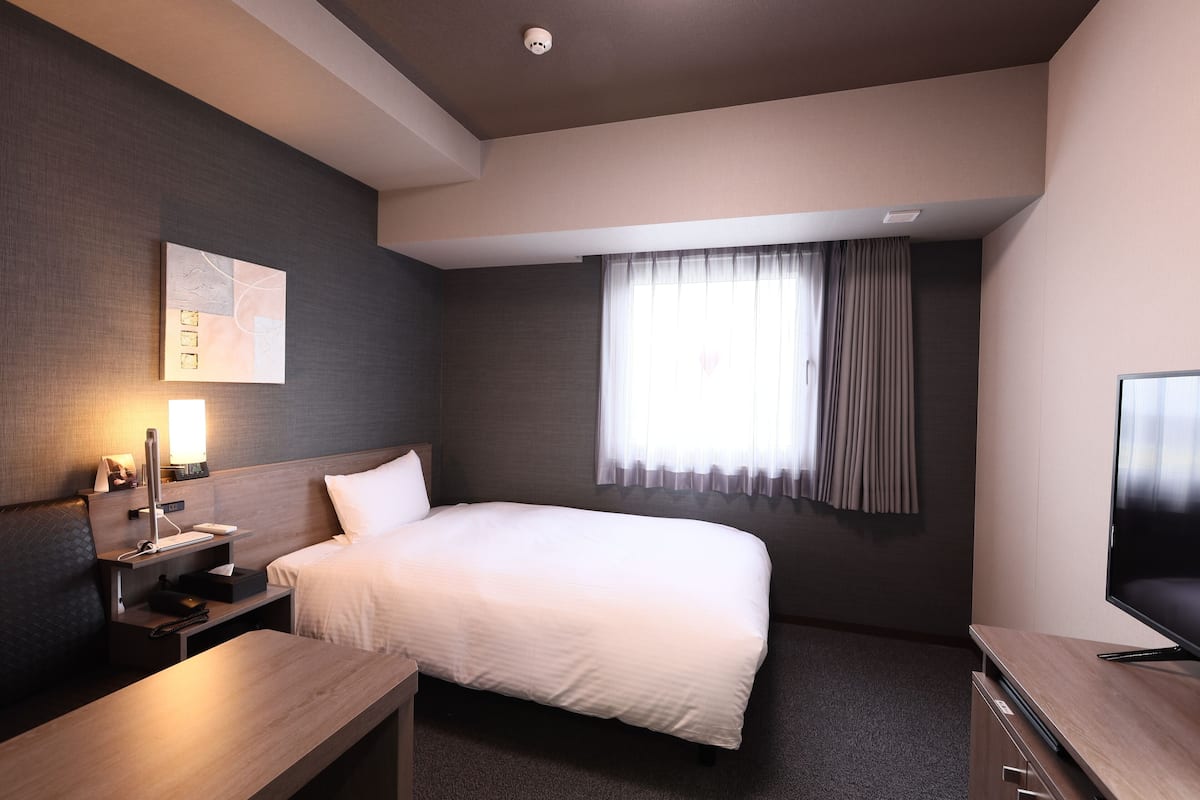 Quarto de hotel moderno com uma cama grande, uma escrivaninha, televisão de tela plana e uma janela com cortinas.