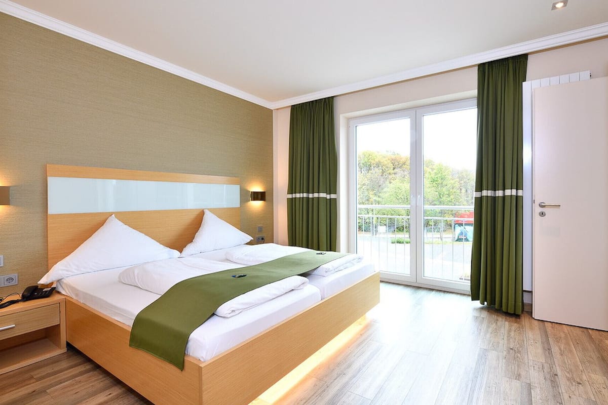 Quarto de hotel com uma cama grande, uma mesa de cabeceira com telefone e vista para o exterior através de uma porta de vidro deslizante.