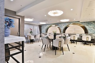 Uma sala de jantar moderna com mesas e cadeiras redondas, piso de mármore e um candelabro.