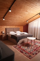 Quarto com teto de madeira, cama com roupa de cama branca, mesa de cabeceira com abajur e tapete estampado.