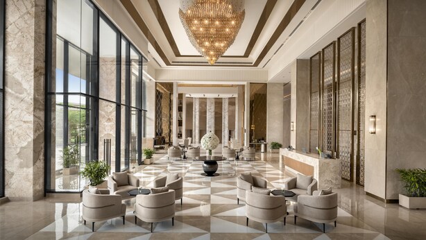 Um hall amplo com um lustre grande, piso de mármore e assentos modernos.