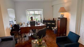 Uma sala de estar com piso de madeira, uma escrivaninha com um laptop, uma cadeira, um sofá e um abajur.