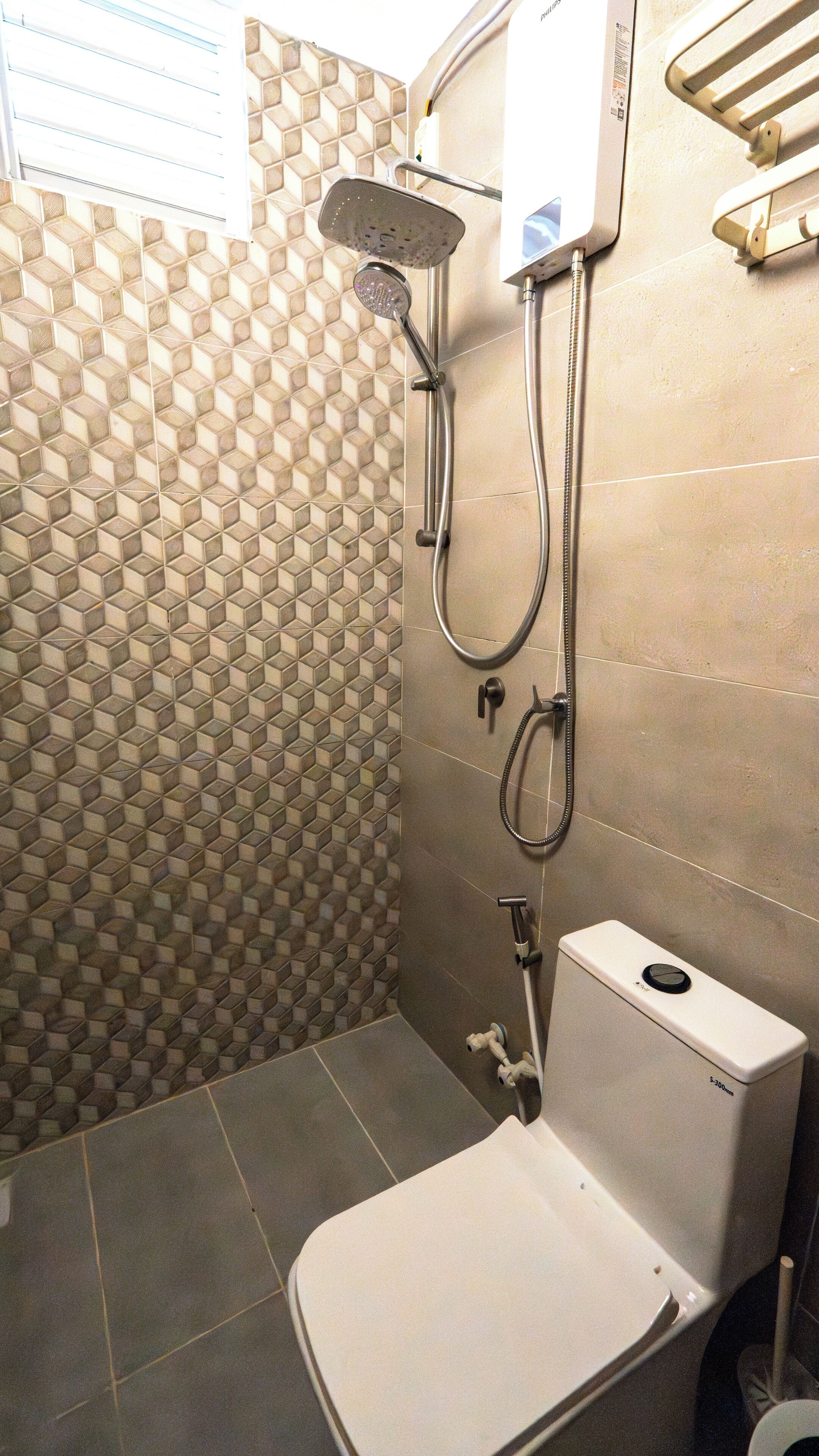 Casa de banho com sanita, chuveiro e parede revestida a azulejos.