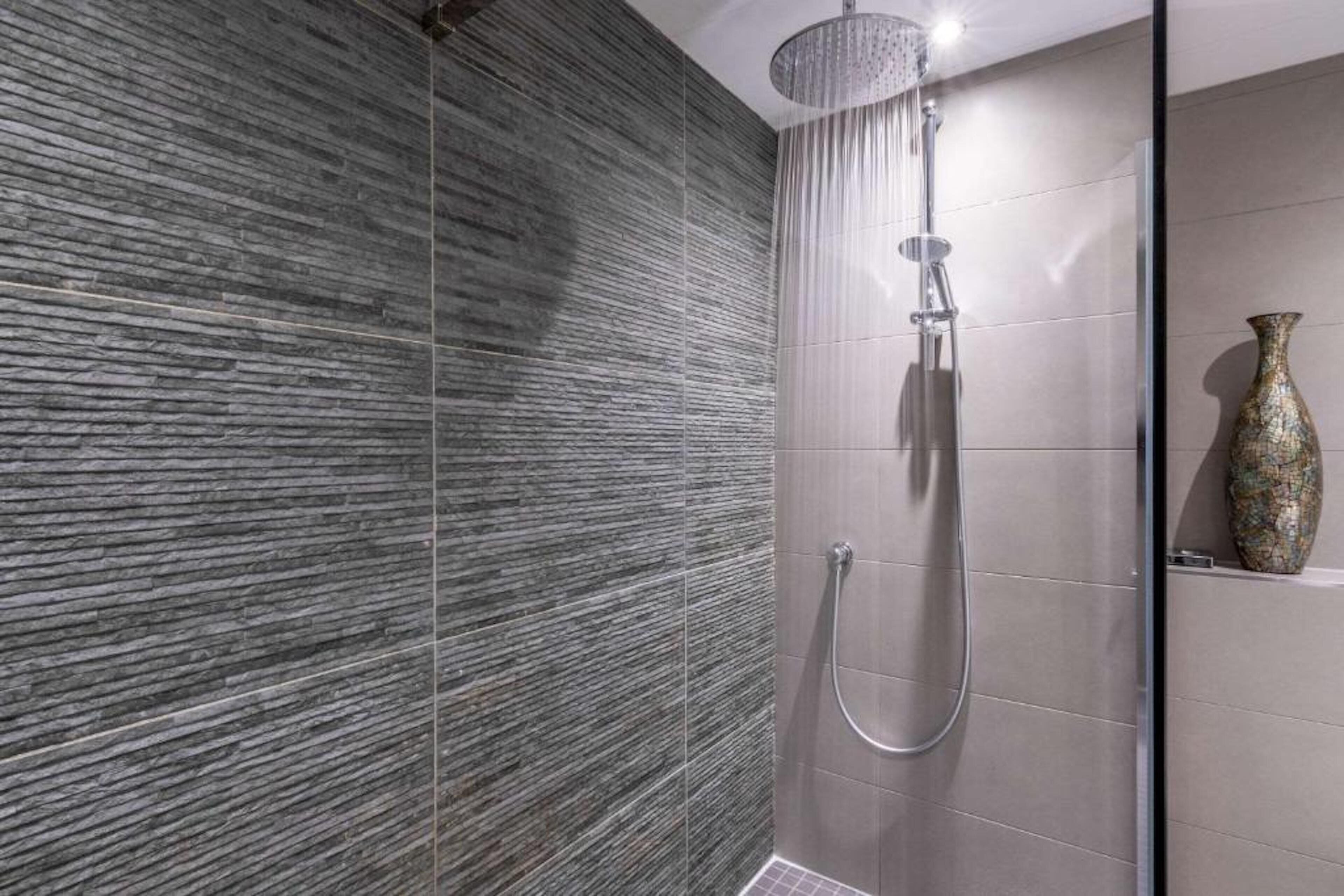 Um chuveiro moderno com um chuveiro de chuva, porta de vidro e um vaso decorativo na parede.