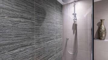 Um chuveiro moderno com um chuveiro de chuva, porta de vidro e um vaso decorativo na parede.