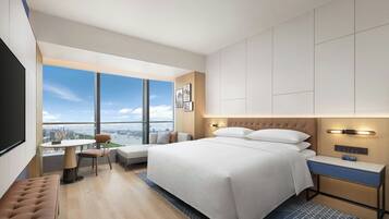 Quarto de hotel moderno com uma cama grande, uma mesa, uma cadeira e vista para a cidade.