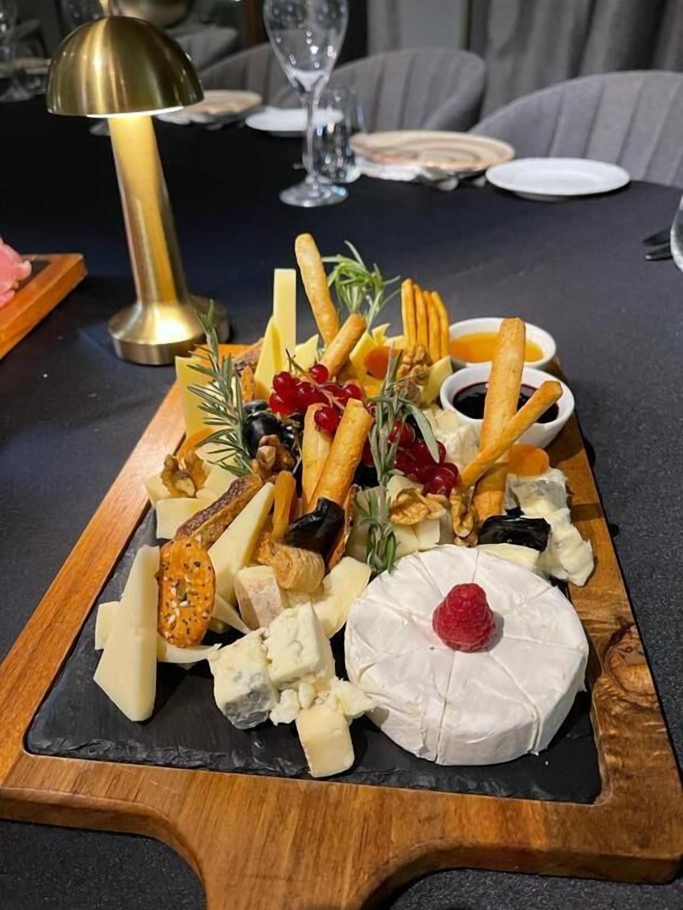 Uma tábua de frios com diversos queijos, frutas, nozes e biscoitos em uma lousa de ardósia.