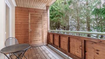 Um deck de madeira com mesa e cadeira de metal, uma porta de madeira e vista para árvores.