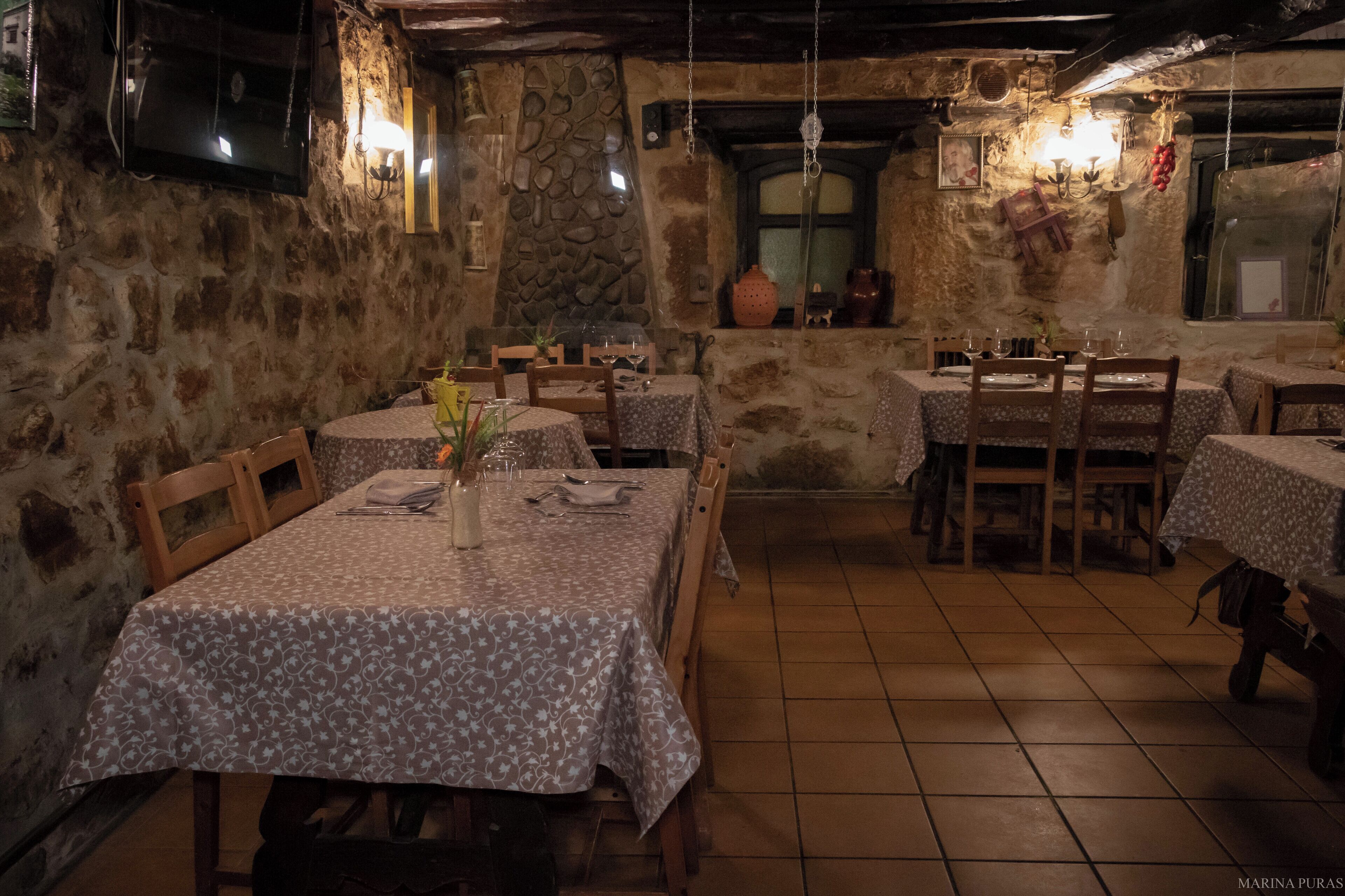 Uma zona de refeições rústica com paredes de pedra, mesas de madeira e toalhas de mesa estampadas.